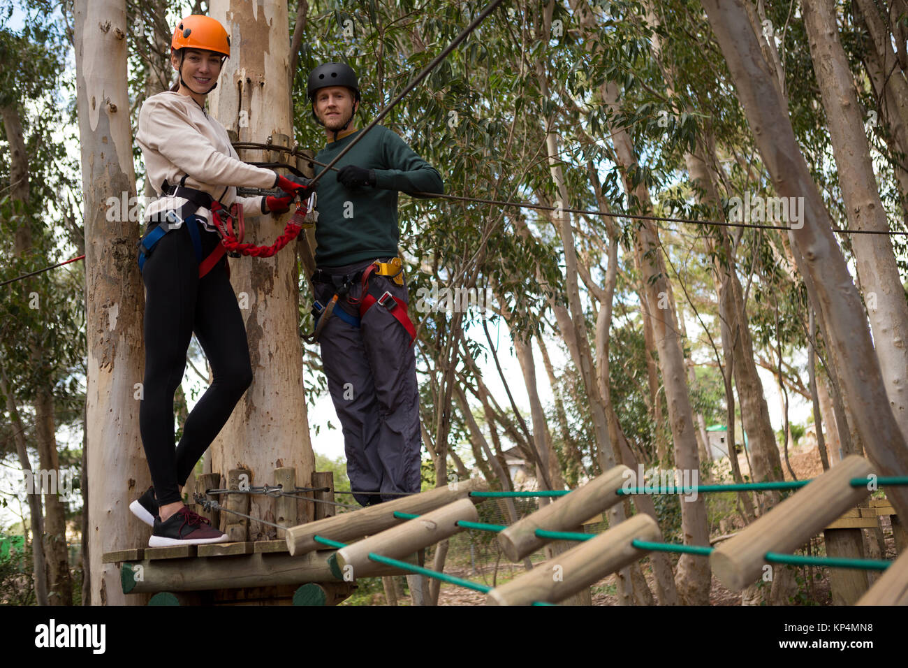 Portrait of smiling couple holding zip line cable standing on wooden ...