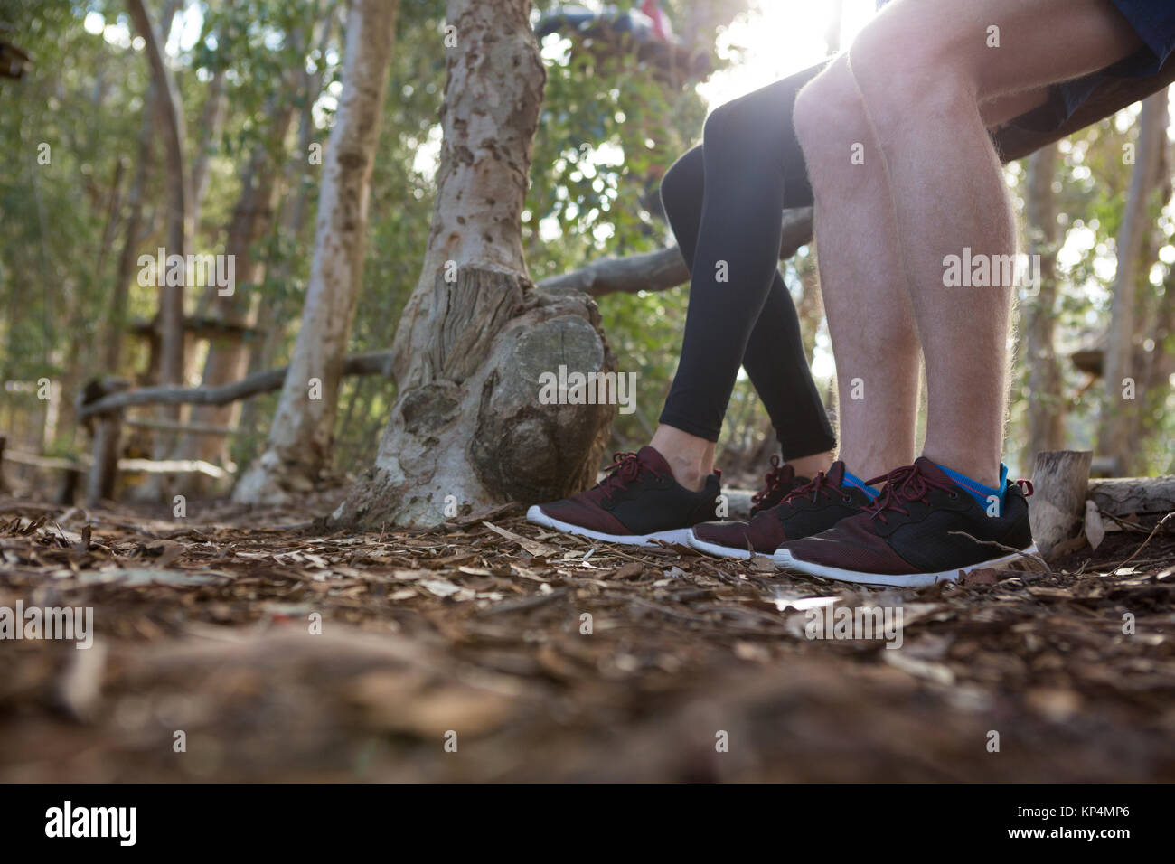 Close-up of legs of man and woman sitting on log of wood in the forest ...