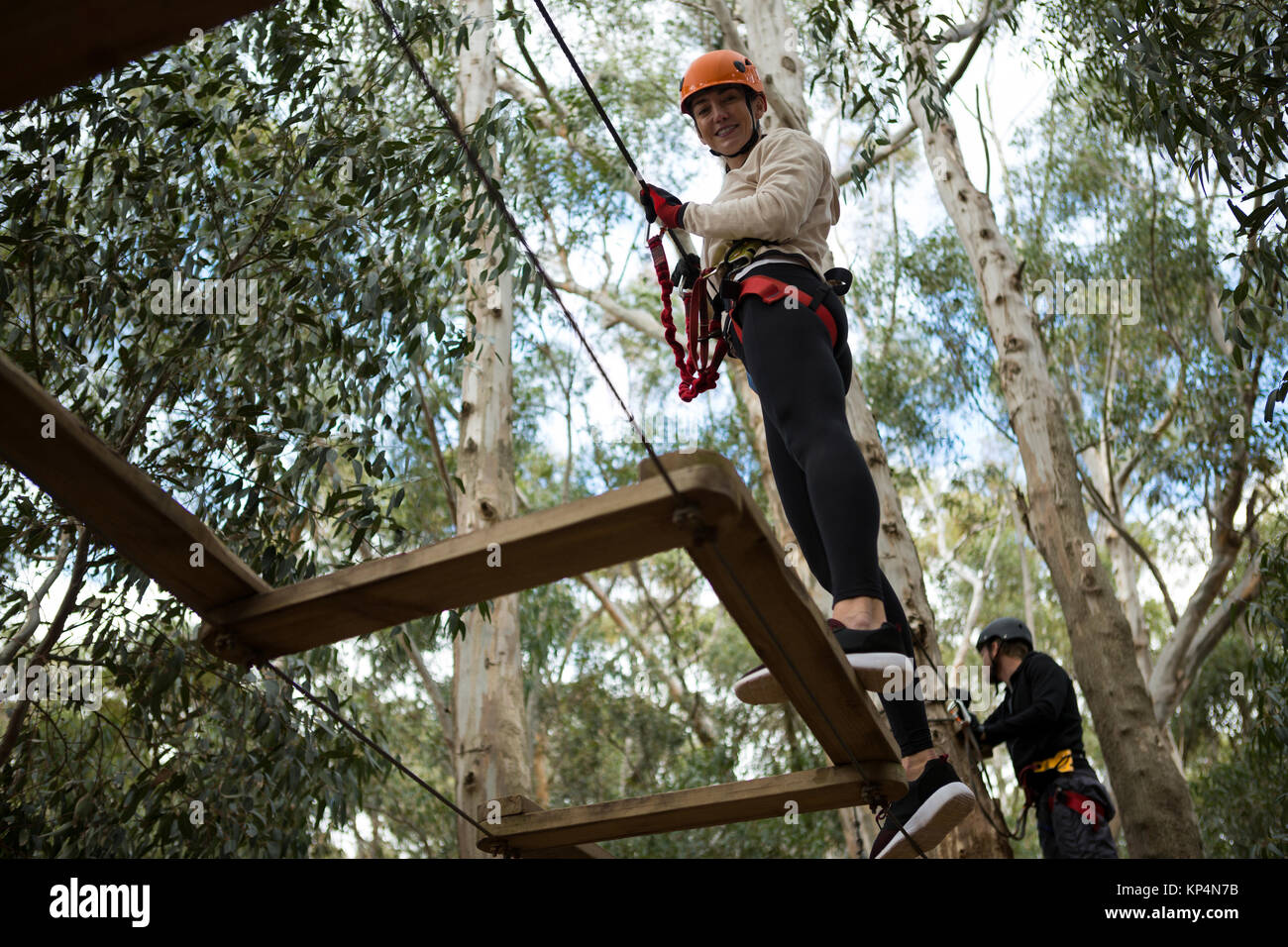 Smiling woman crossing zip line and man standing near zip line in the ...