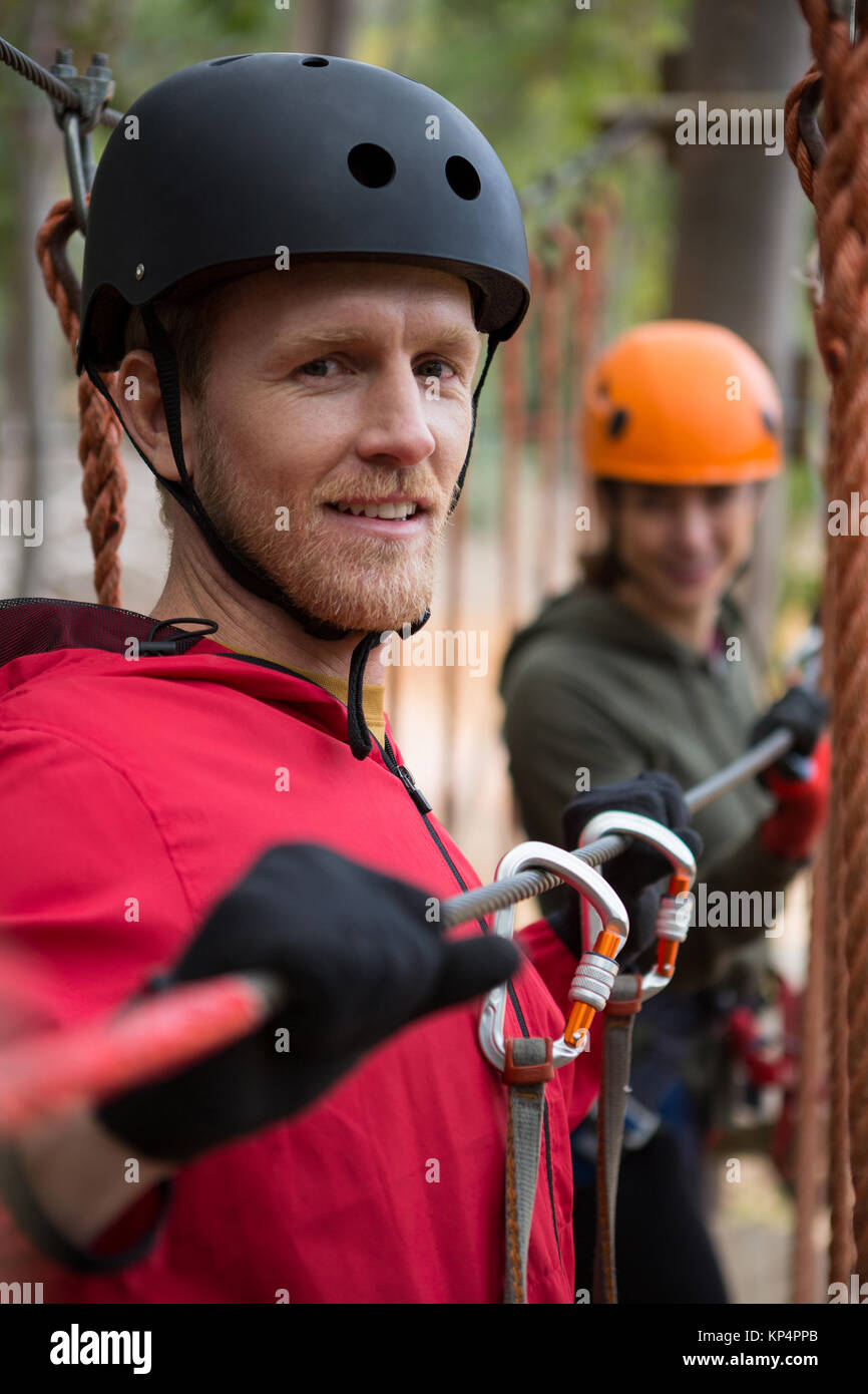 Portrait of smiling young man wearing safety helmet holding zip line ...