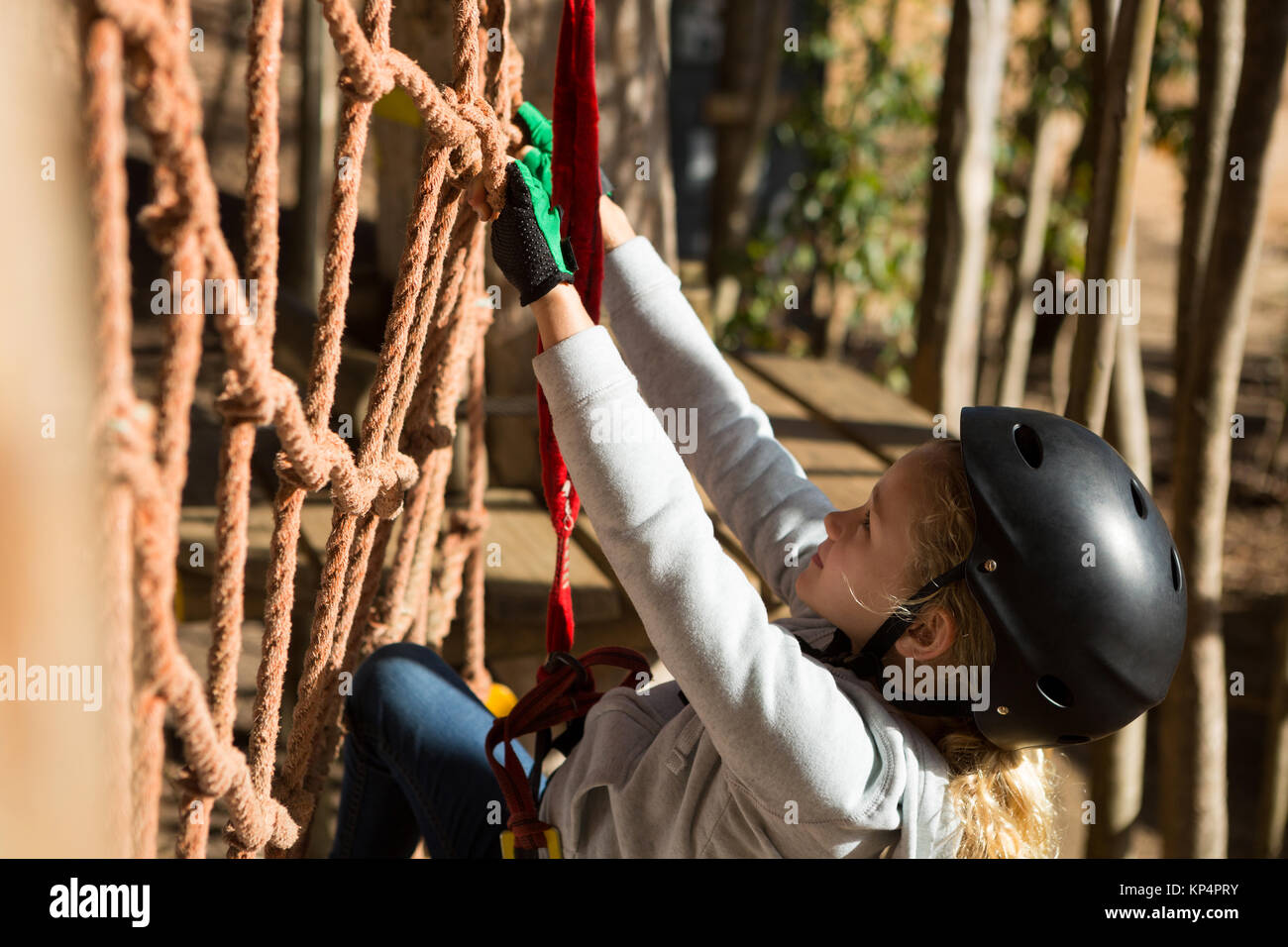Close-up of little girl wearing helmet climbing on rope fence in the ...