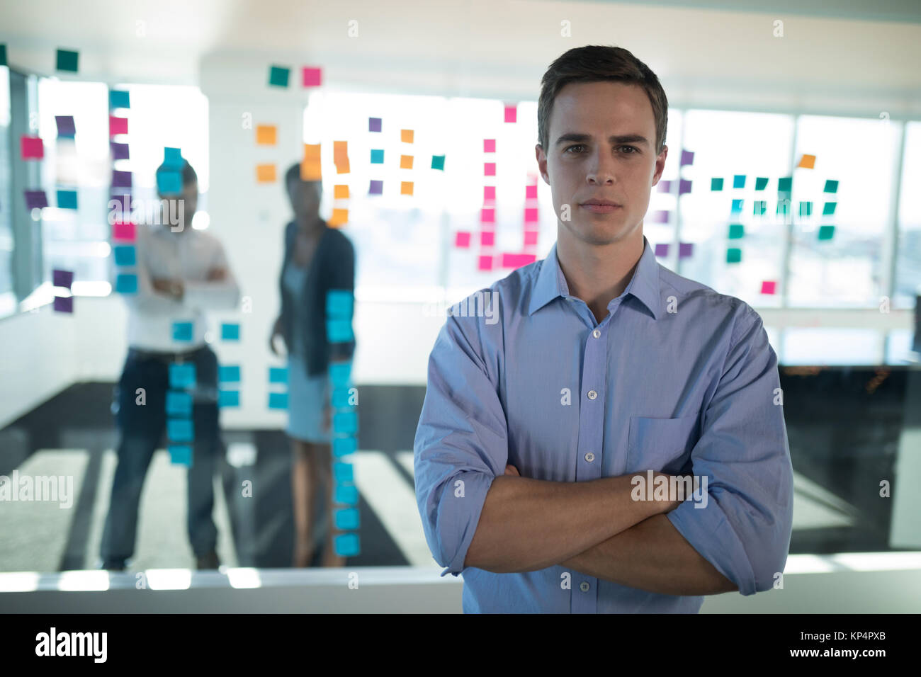 Portrait of male executive standing in office with colleagues in ...
