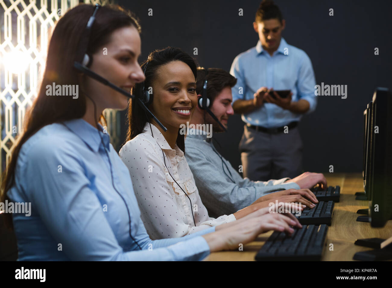 Business executives with headsets using computers at desk in office ...