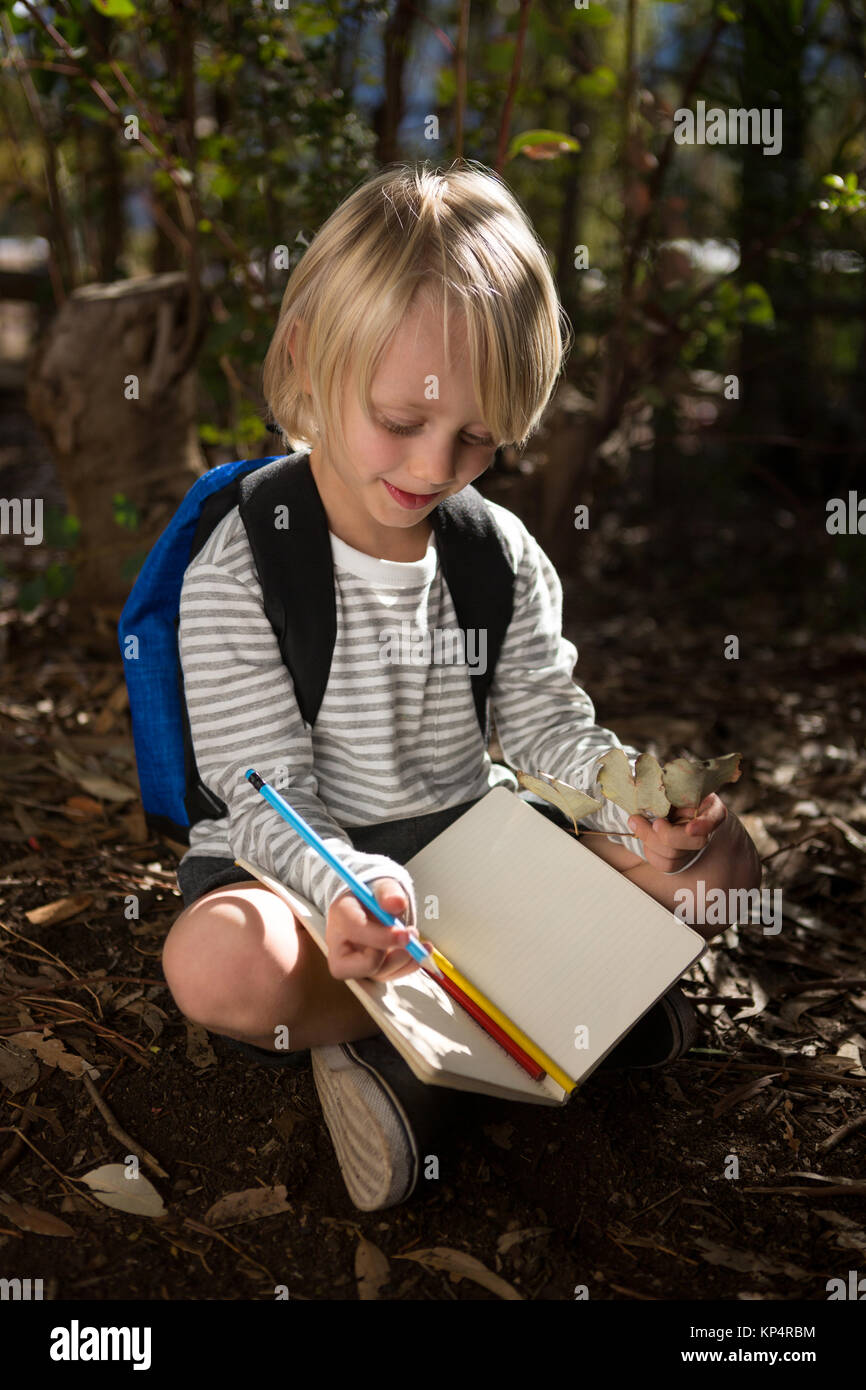 Close-up of little girl with backpack sitting on ground writing in ...