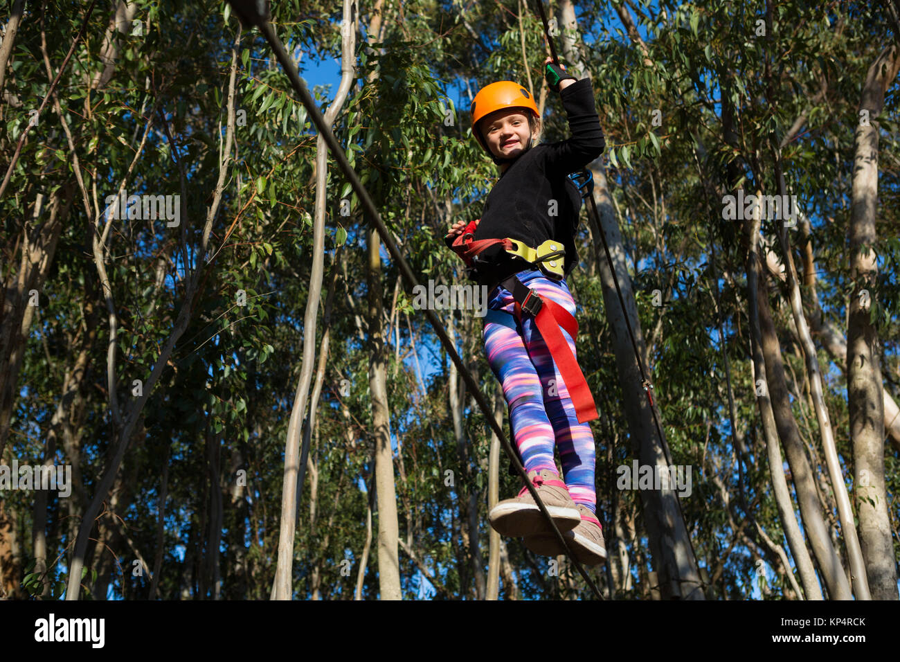 Little girl wearing helmet crossing zip line in the forest Stock Photo ...