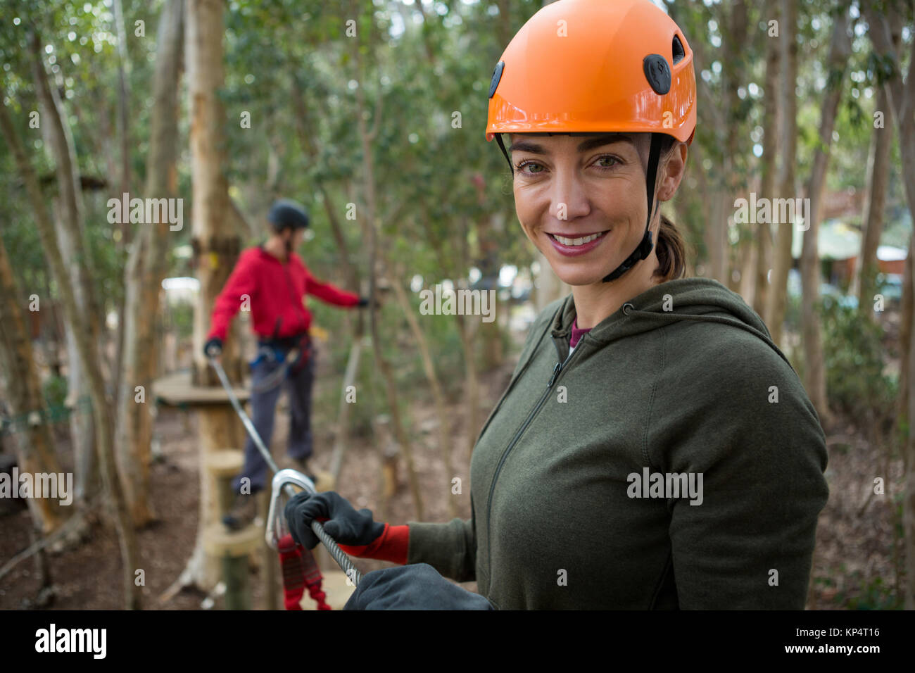 Portrait of smiling young woman holding zip line cable and standing in ...