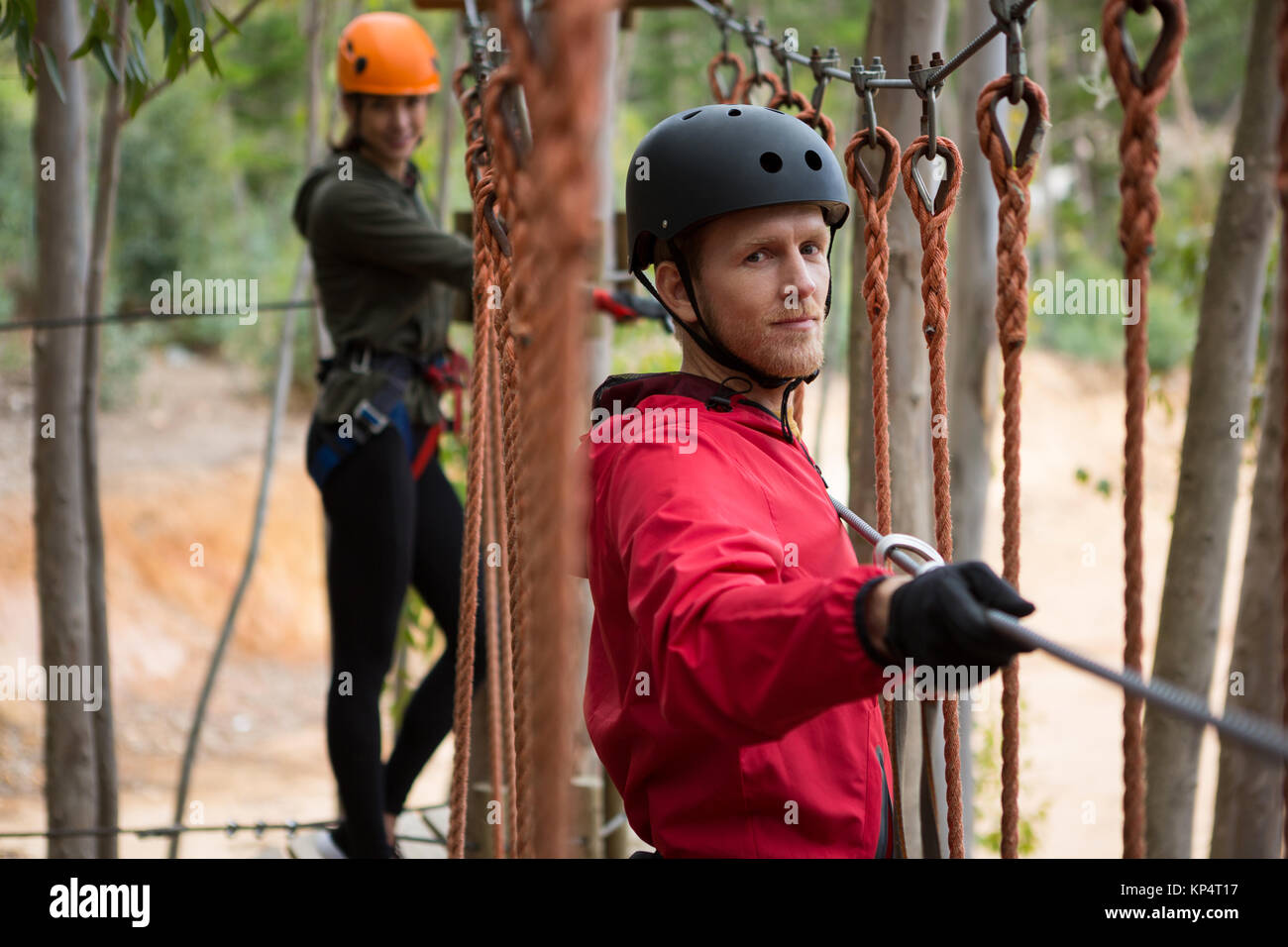 Smiling young man wearing safety helmet crossing zip line cable in ...