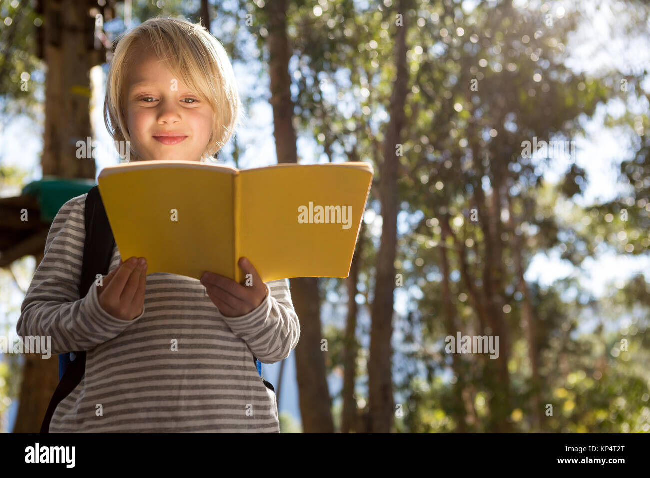Little girl with a backpack reading a book in the forest Stock Photo ...