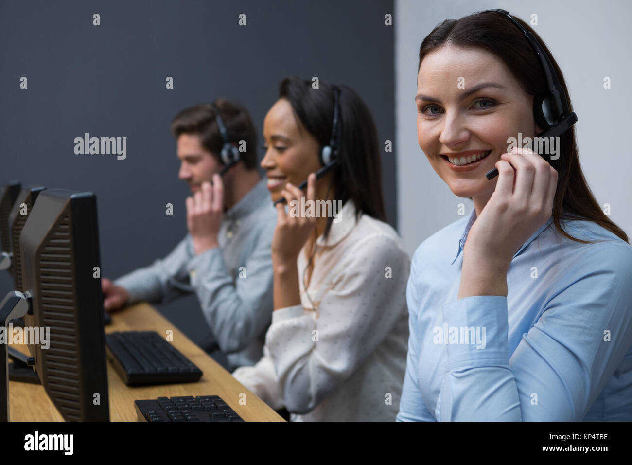 Business executives with headsets using computers at desk in office ...
