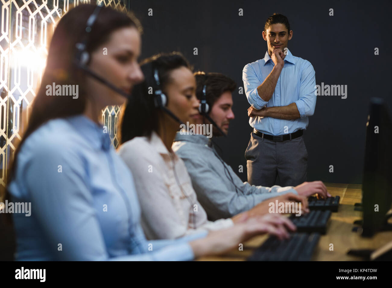 Business executives with headsets using computers at desk in office ...
