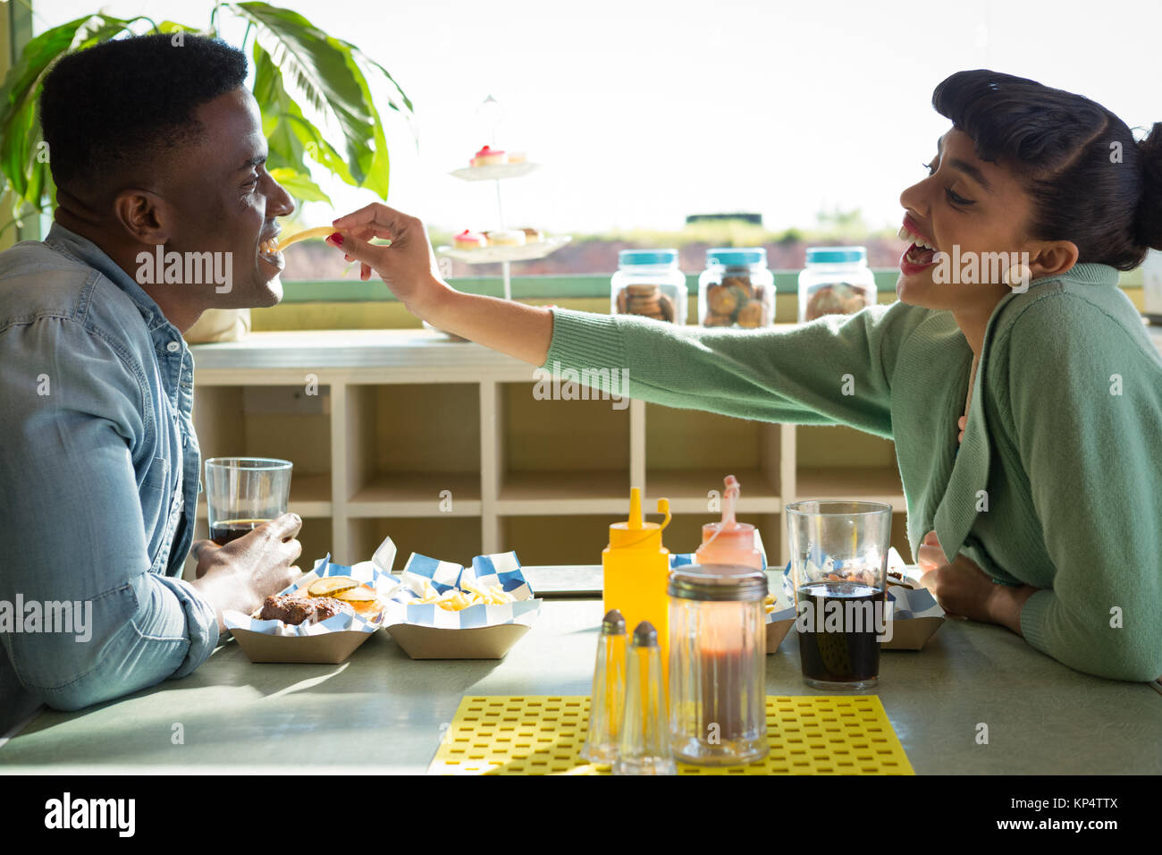 Happy couple sitting together in restaurant while woman feeding food ...