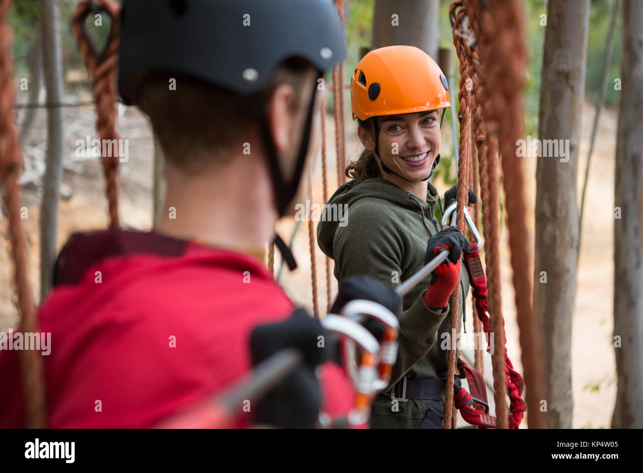 Smiling young woman looking at man while crossing zip line in the ...