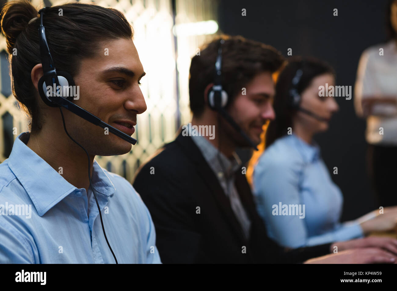 Business executives with headsets using computers at desk in office ...