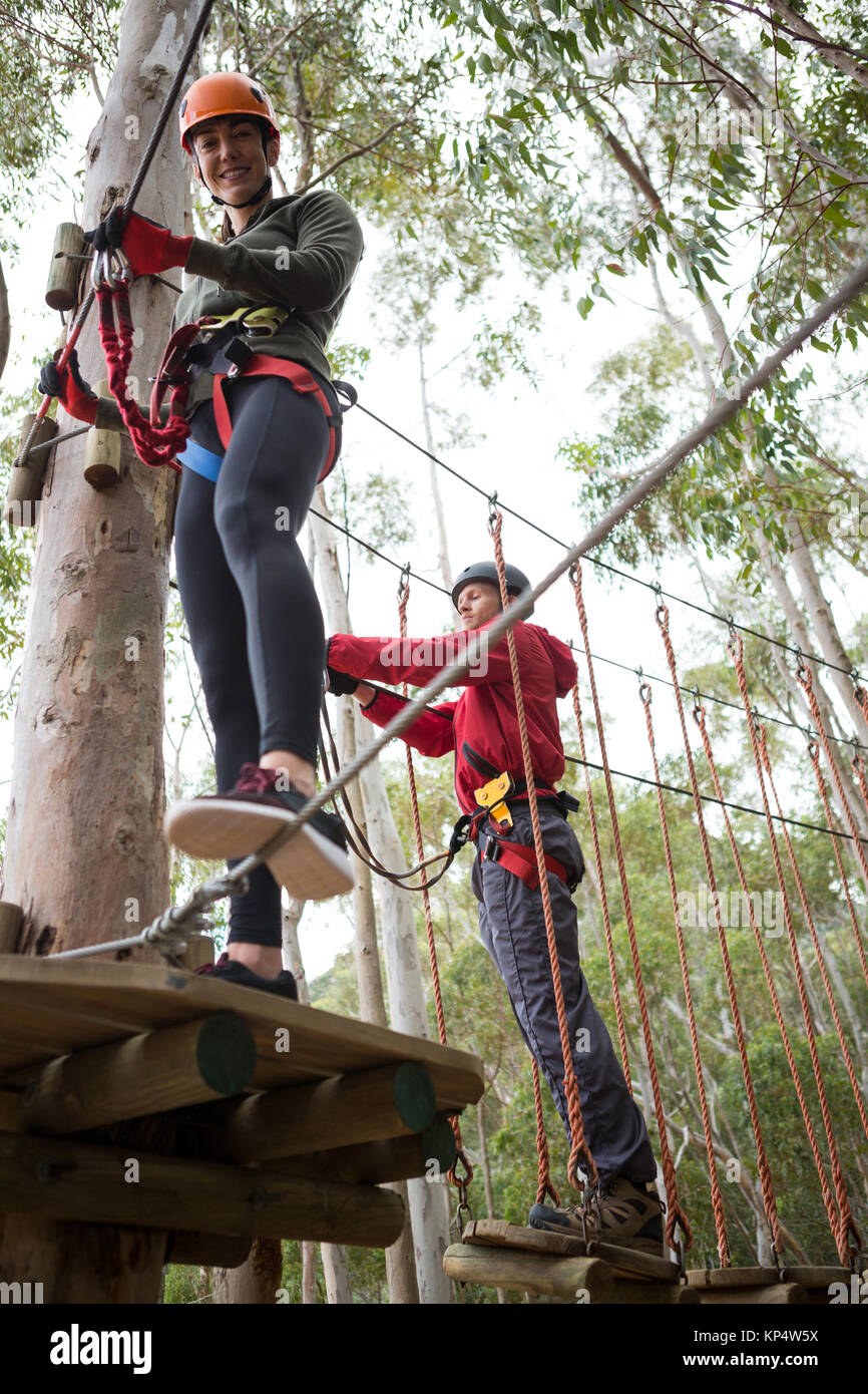 Young woman climbing on zip line while man fixing his harness on cable ...