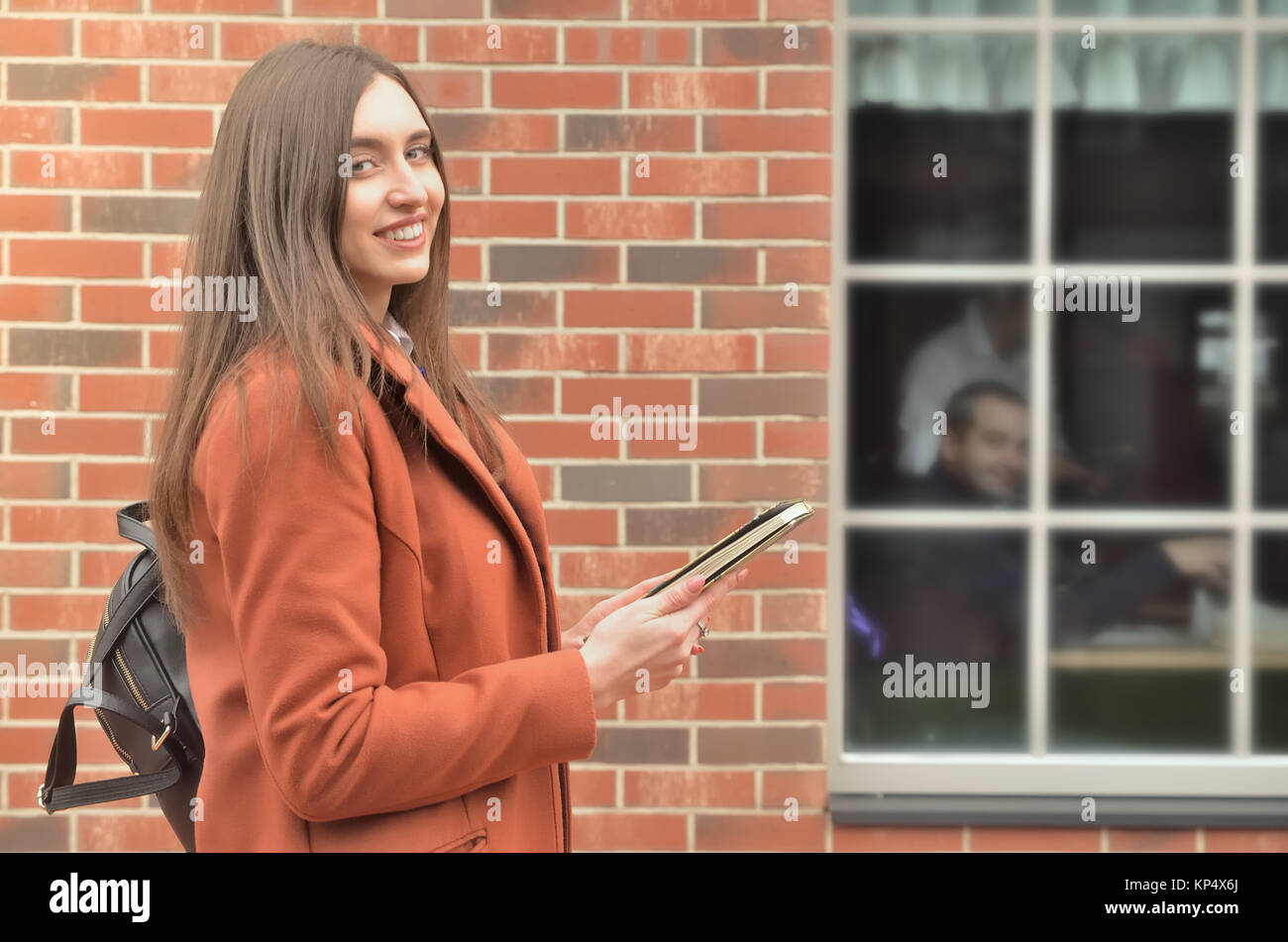A beautiful girl stands against the backdrop of a building, holding a ...