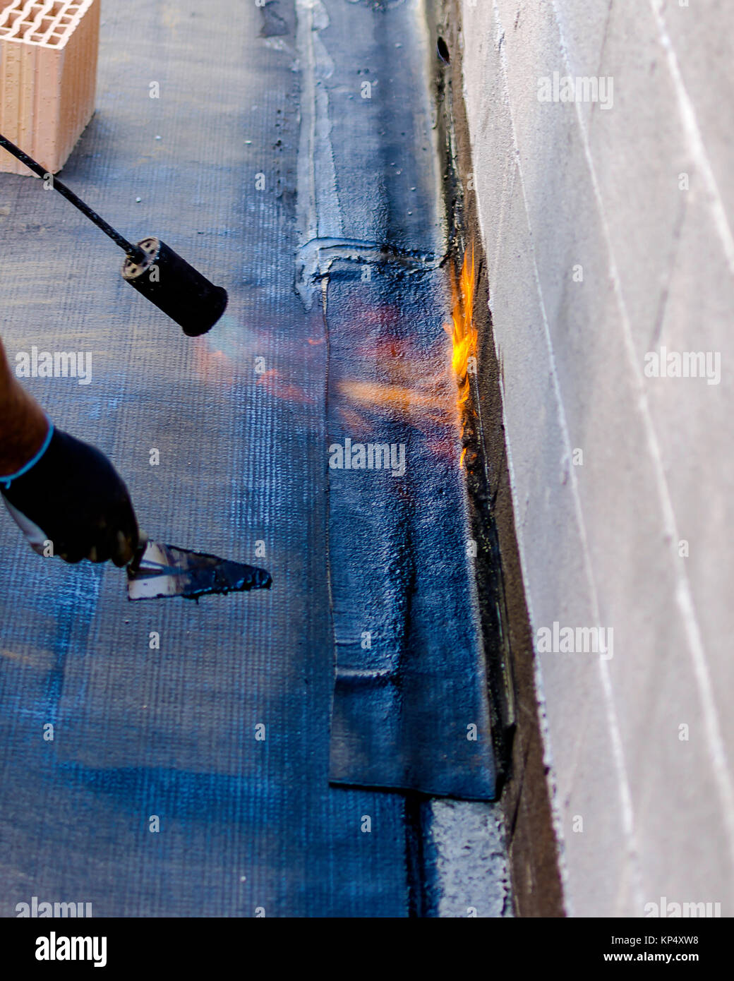 Roofer installing rolls of bituminous waterproofing membrane for the waterproofing of a terrace ...