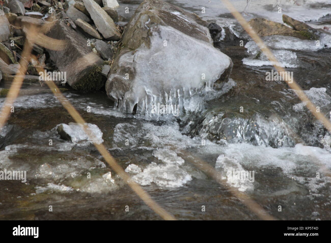 Ice forming on rocks near the bank of a cascading waterway at the start ...