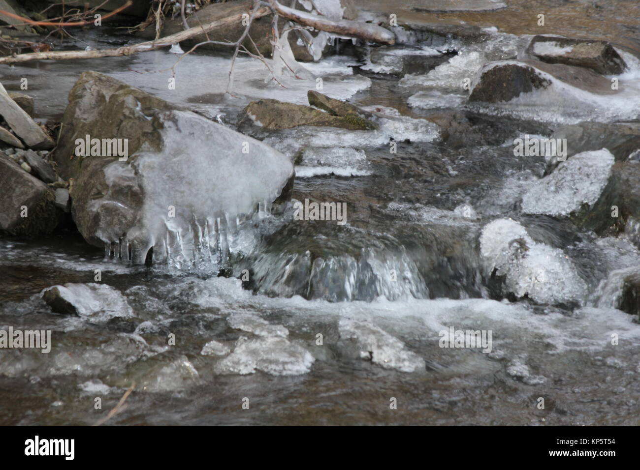 Ice forming on rocks near the bank of a cascading waterway at the start ...