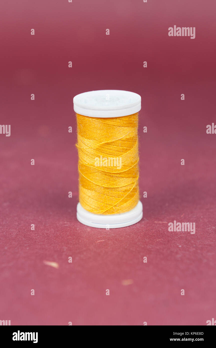 Small yellow sewing thread on red background Stock Photo - Alamy