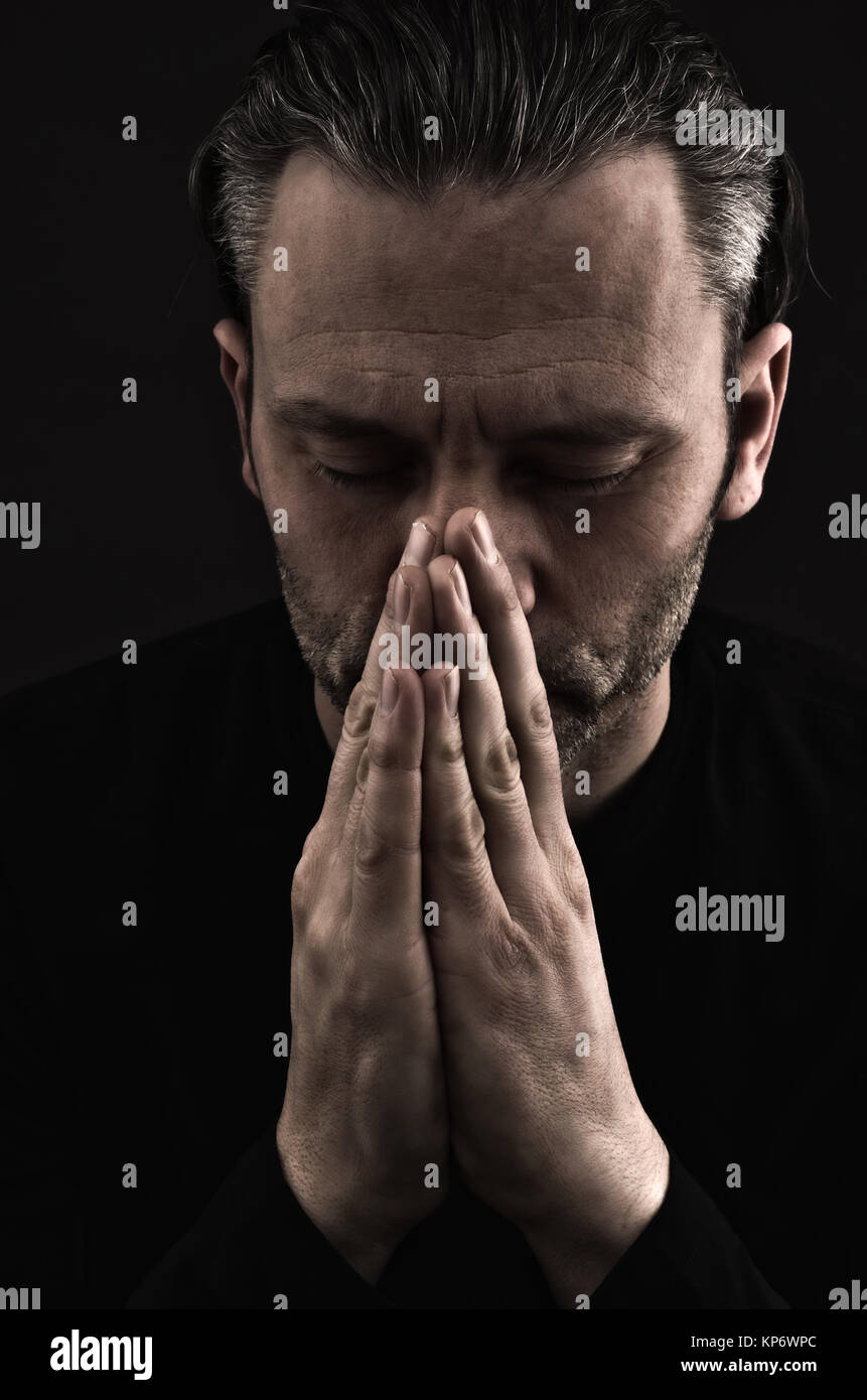 Portrait of sad man praying on a dark background Stock Photo - Alamy