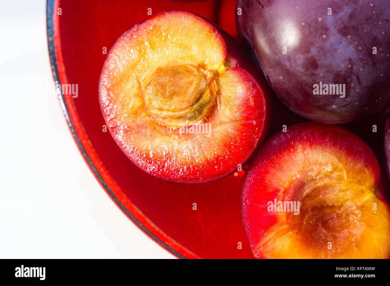 fresh plum fruit with cut plum slices in the red saucer on white ...