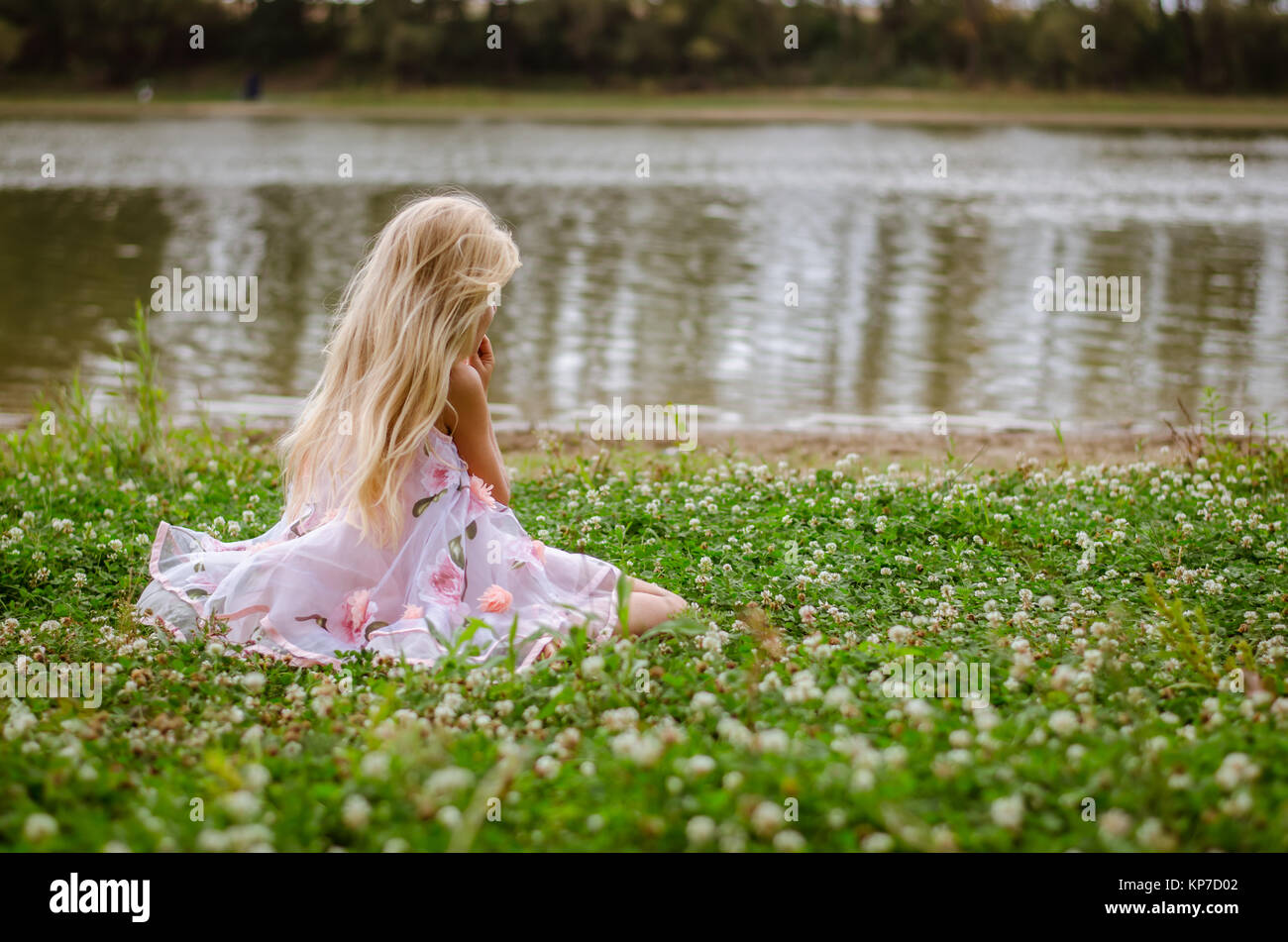 sad lonely girl with long blond hair in pink dress sitting back view ...