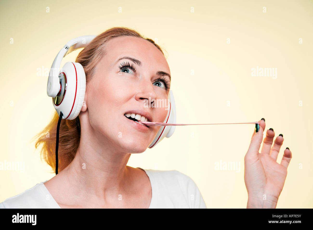 blonde girl with headphones blowing up a bubble of gum on a yellow ...