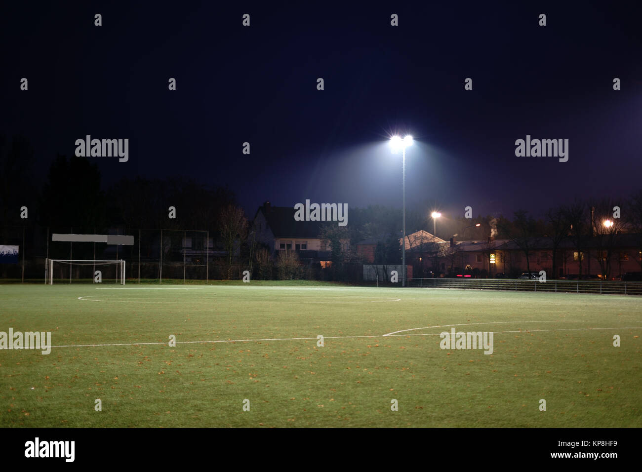 The green lawn of a football field at night is illuminated by ...