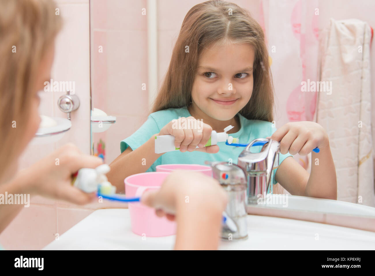 Happy little girl squeezes the toothpaste from a tube on toothbrush ...