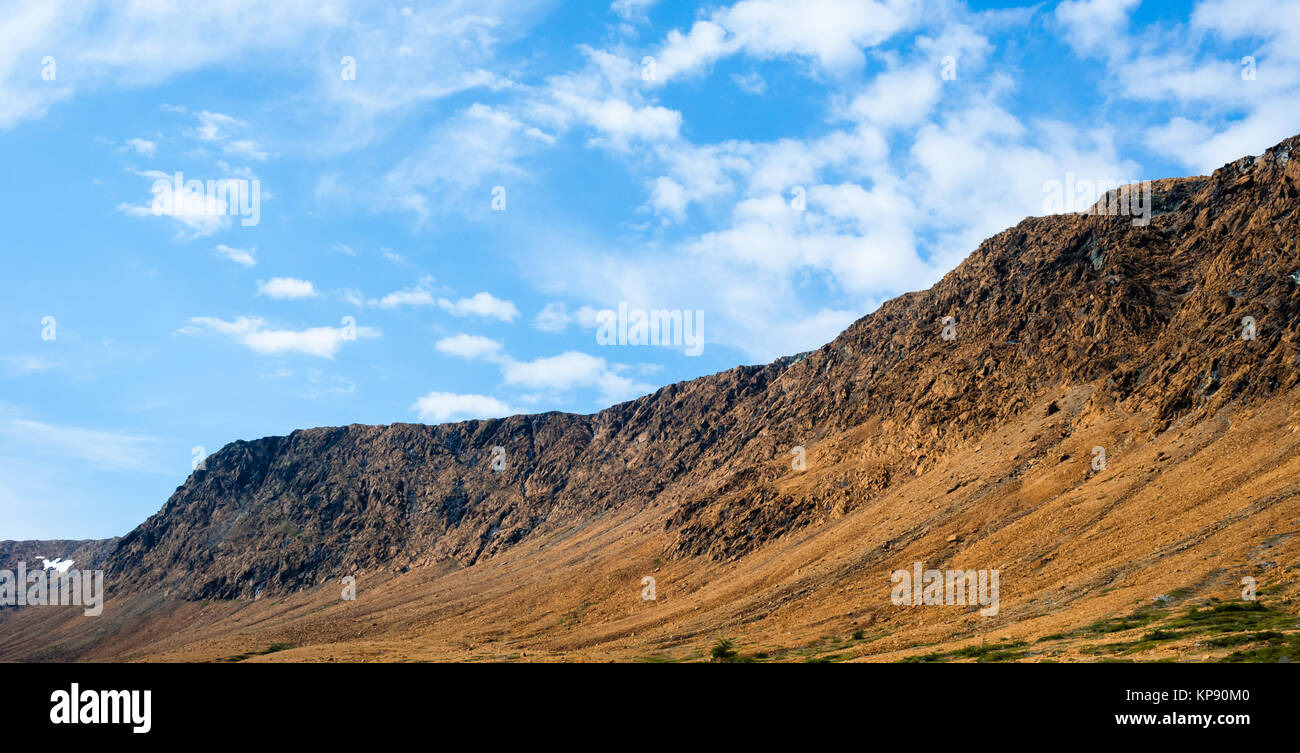 Rocky dry yellow cliff slope against light blue sky Stock Photo - Alamy