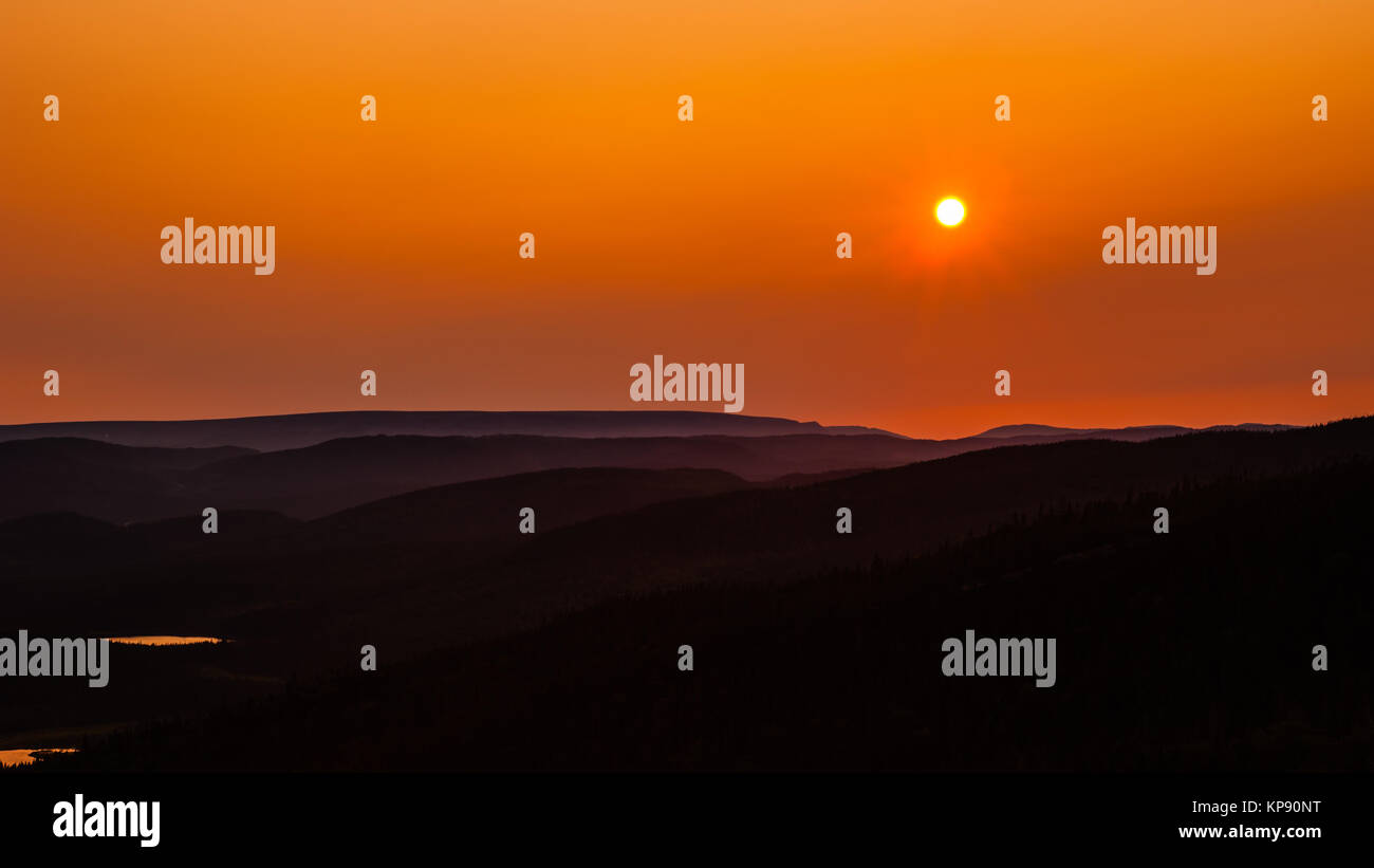 Setting orange sun over hills receding into hazy distance Stock Photo ...