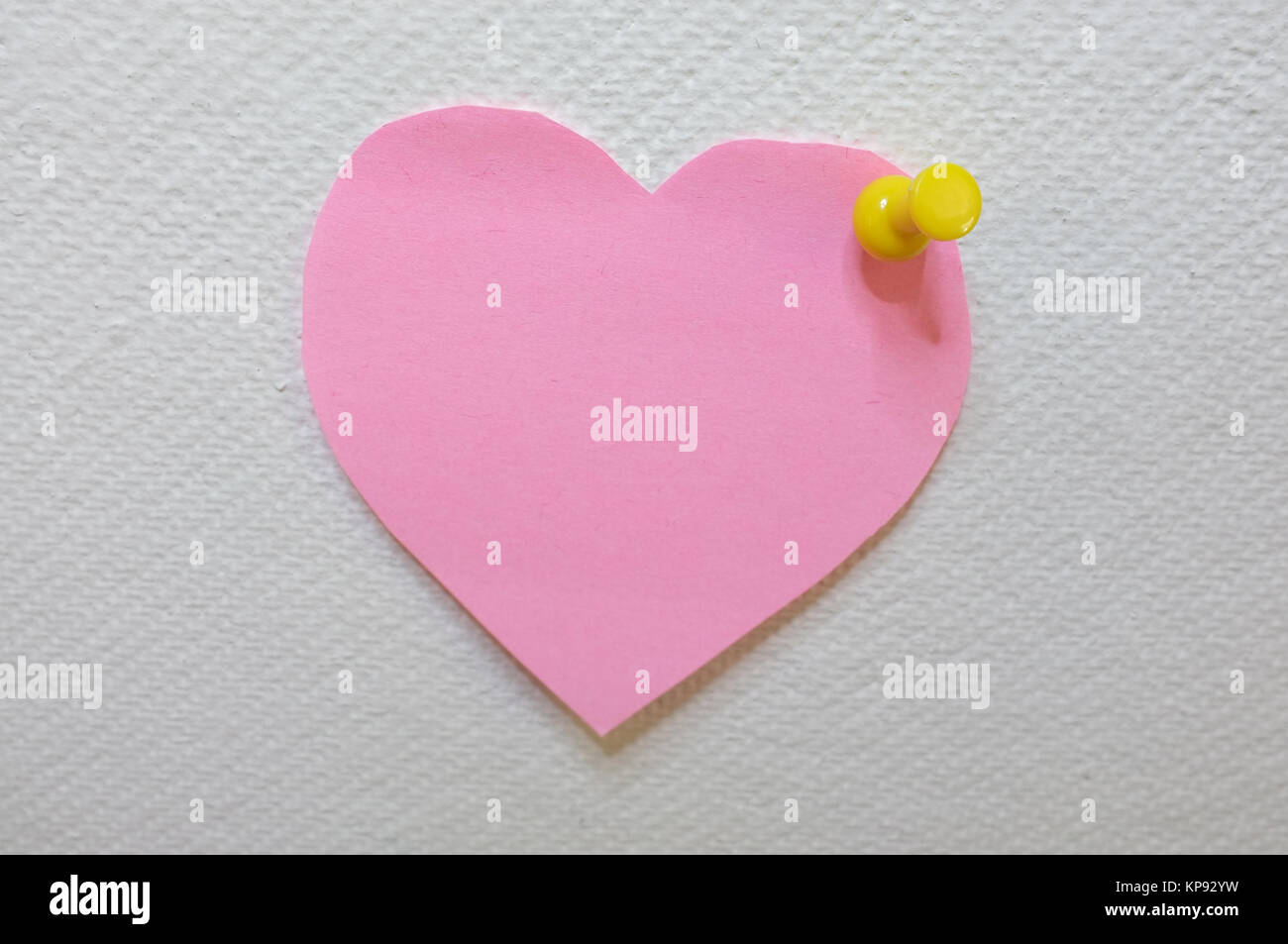 Note paper in heart shape with yellow pin posted on white cork board ...