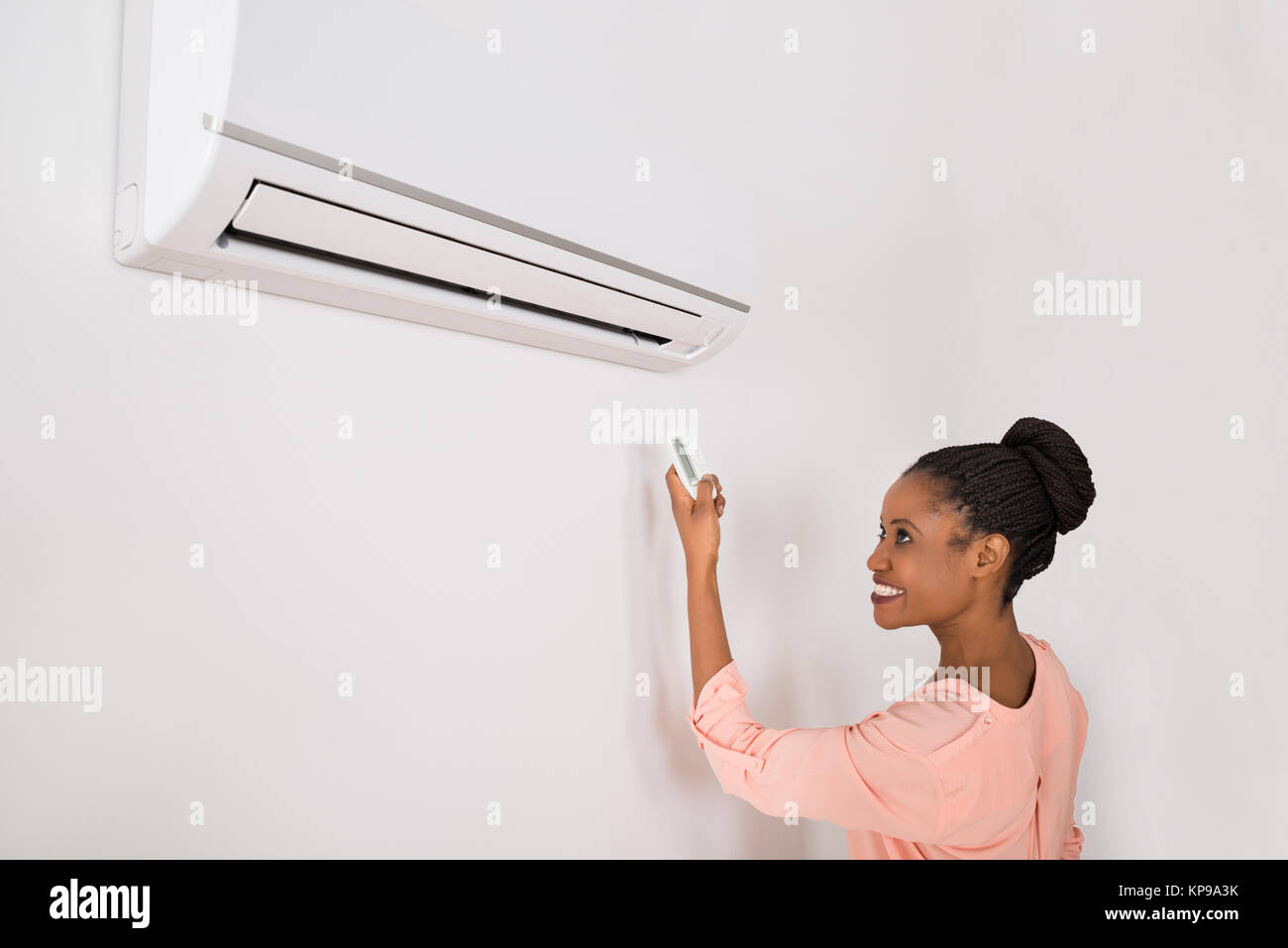 Smiling Woman Operating Air Conditioner Stock Photo - Alamy