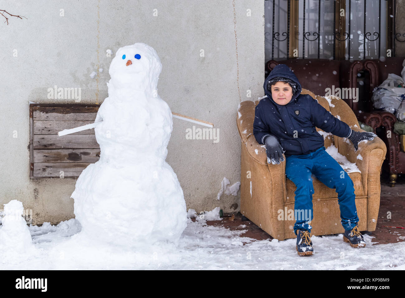 Child sits on a couch after he finished snowman. slide on snow in old ...