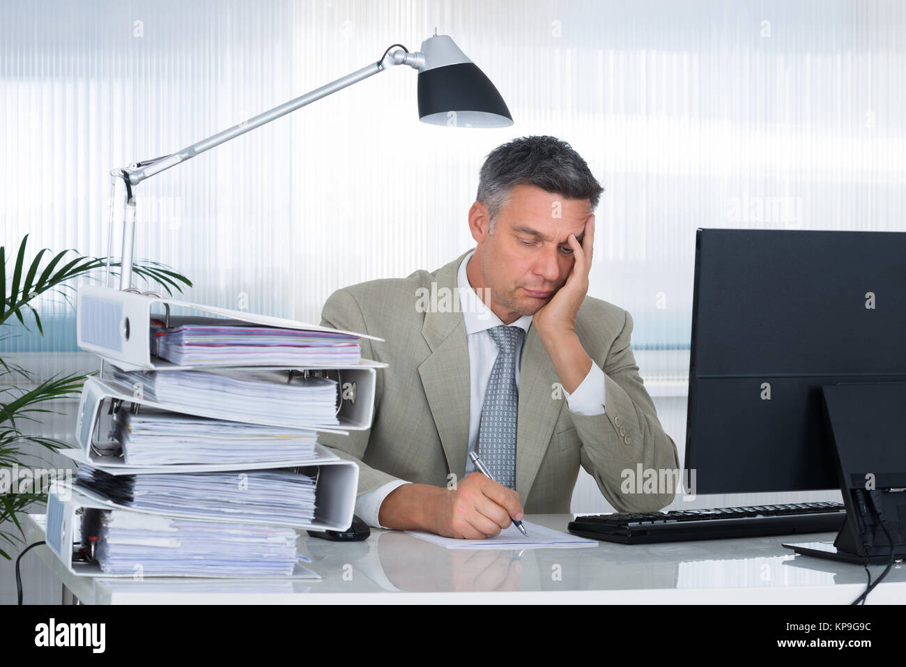 Tired Businessman Writing On Document In Office Stock Photo - Alamy