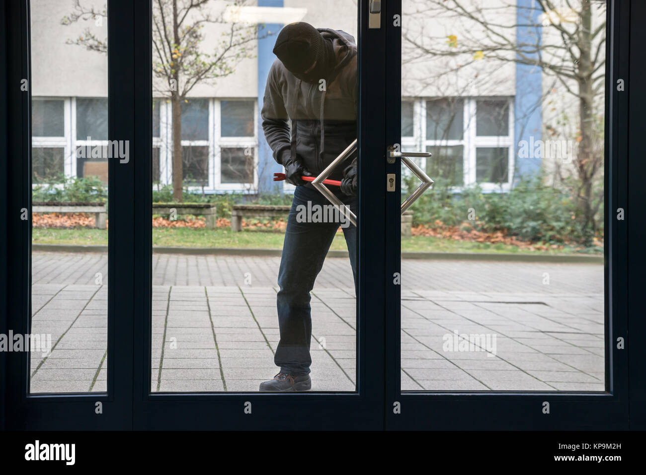Hooded Man Using Crowbar To Open Glass Door Stock Photo - Alamy