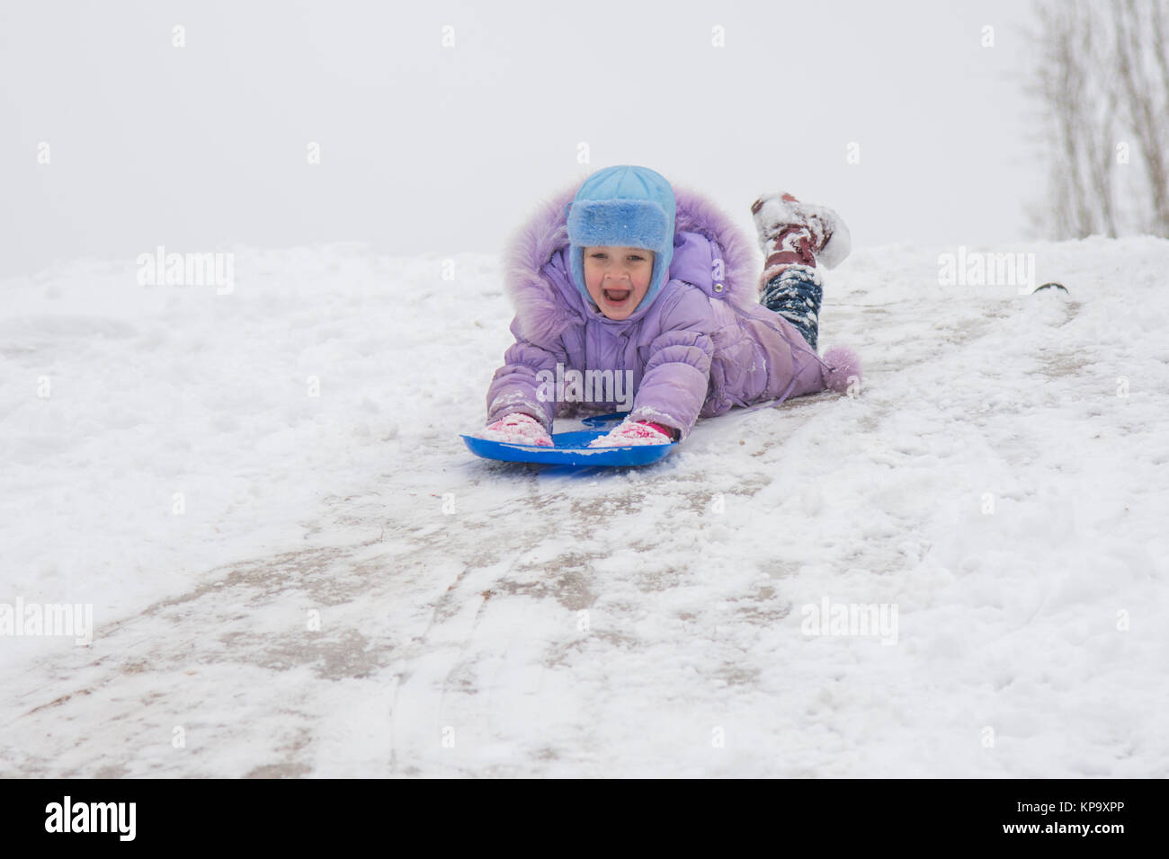 Girl rolls down on his stomach with a headfirst slide snow Stock Photo ...