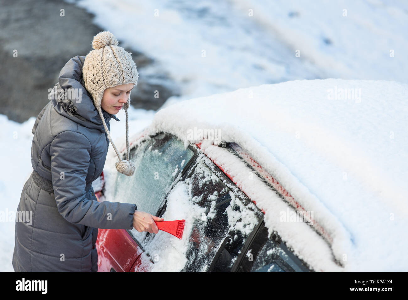 Young woman cleaning her car from snow and frost on a winter morning ...