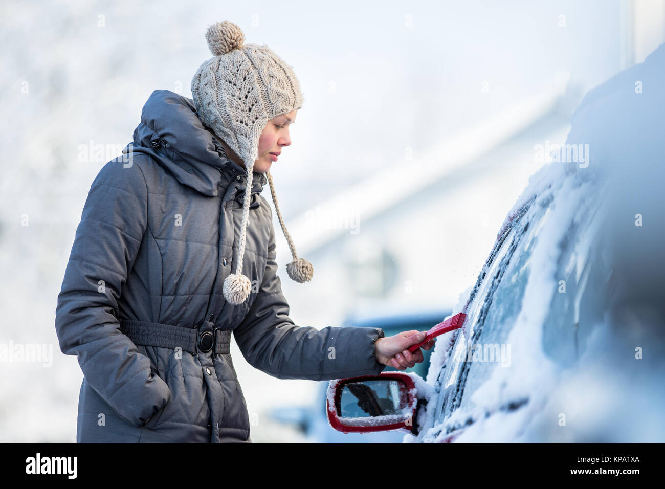 Young woman cleaning her car from snow and frost on a winter morning ...