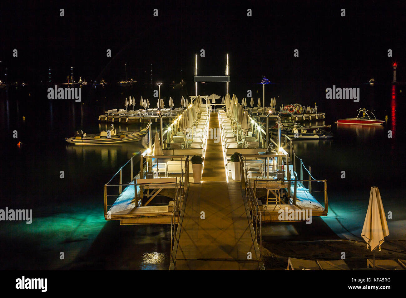 Wooden pier in evening light with its lights on tables, in background ...