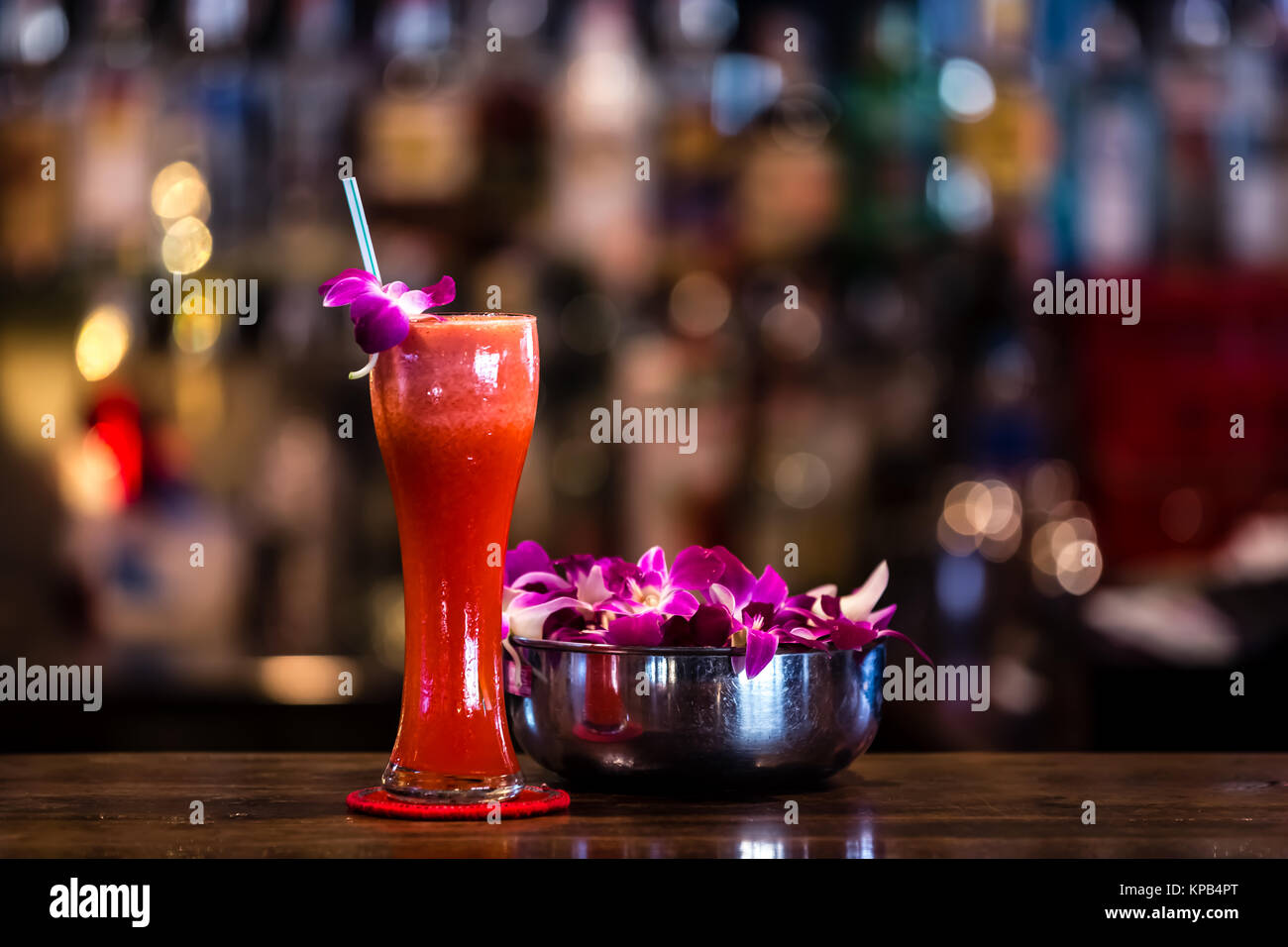 Red cocktail with orchid flower in the bar on the blurred background ...