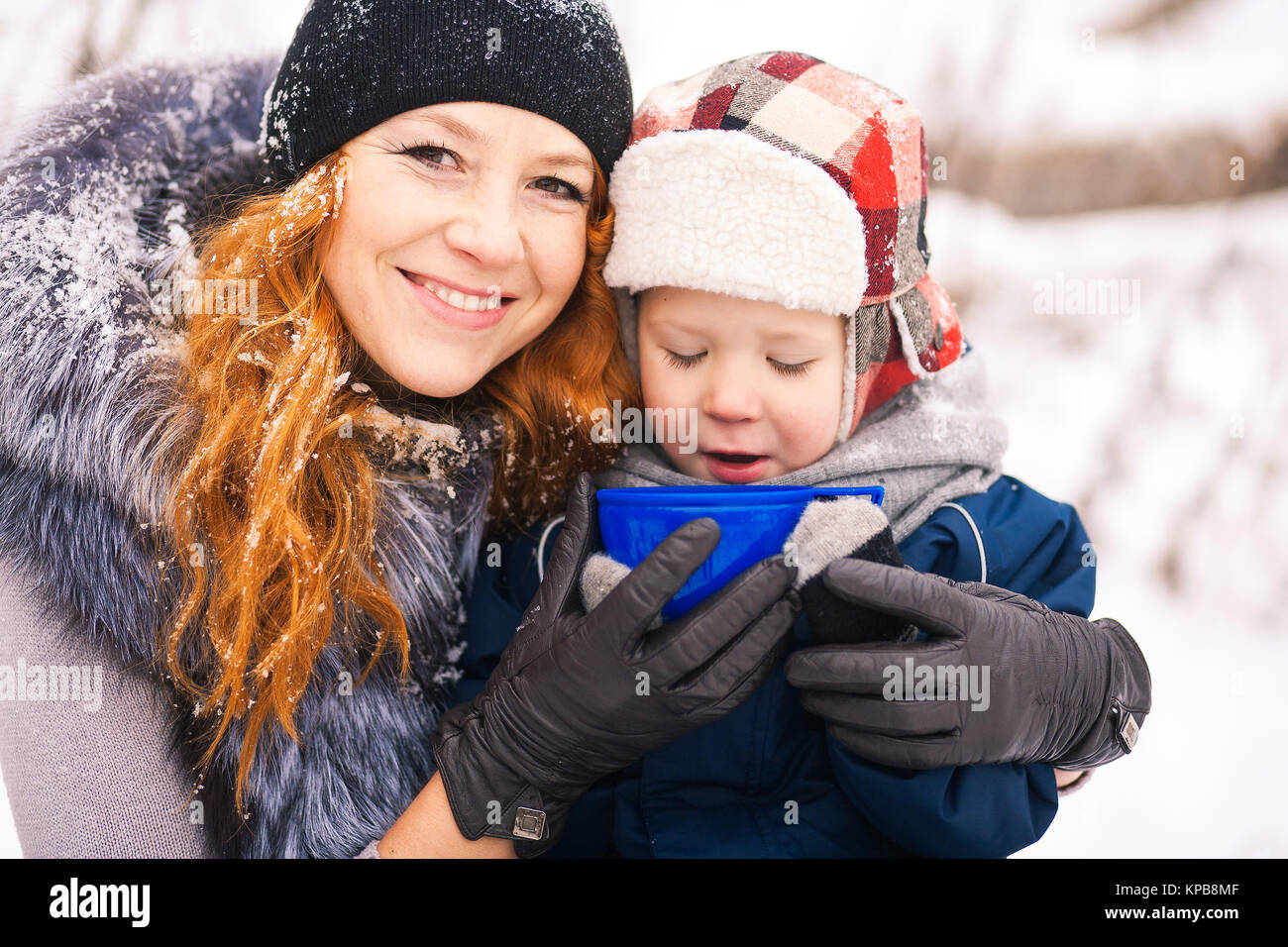 Baby sitting with young beautiful mother outside at snowy trees winter ...