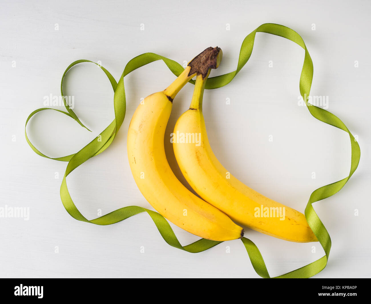 Two bananas with green ribbon frame and heart symbol on white ...