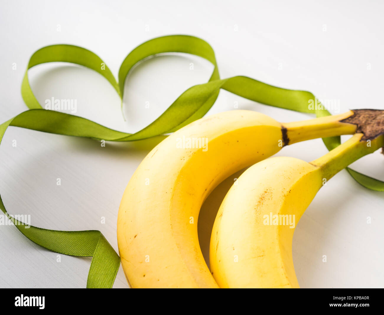 Two bananas with green ribbon frame and heart symbol on white ...