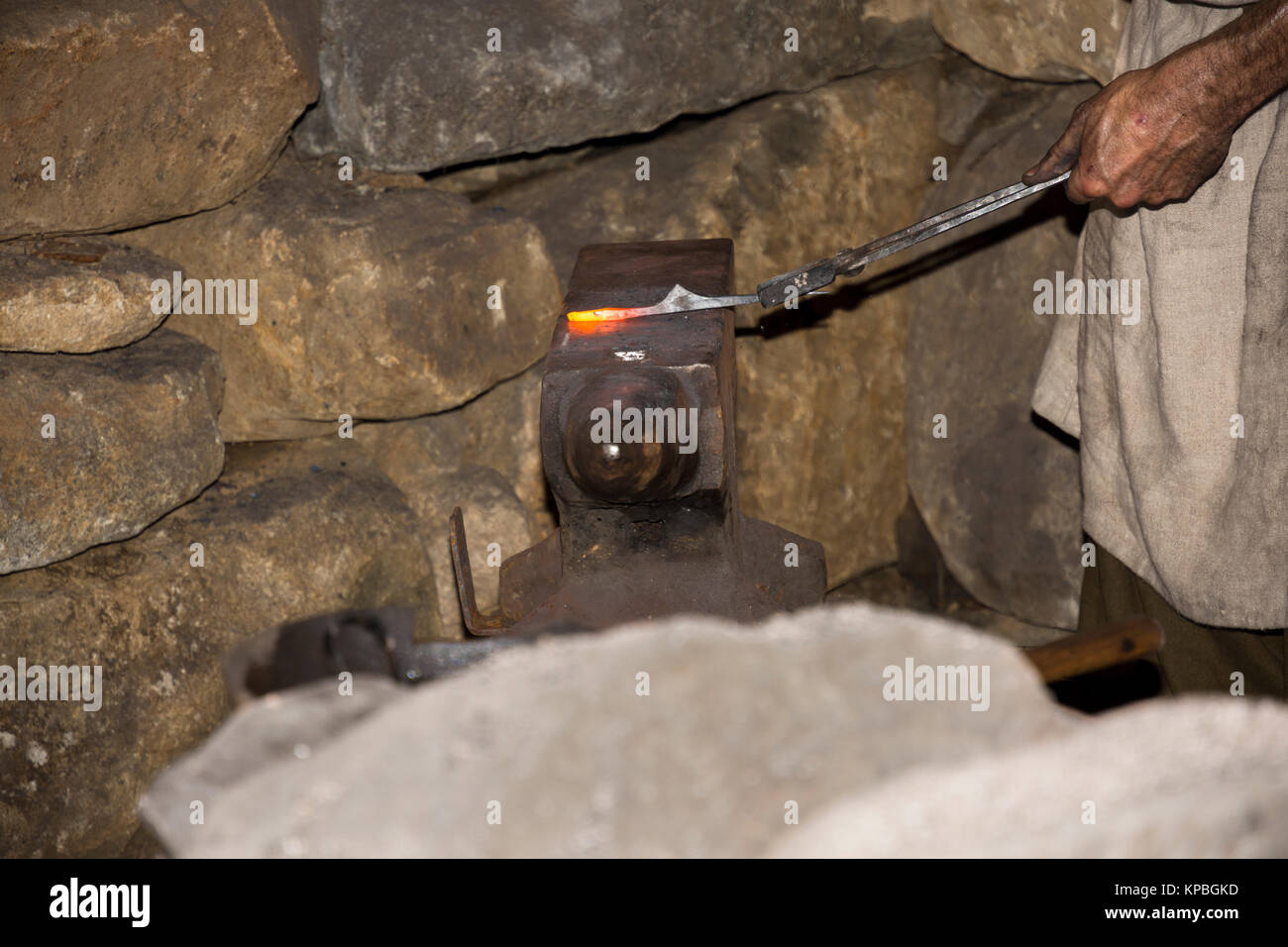 blacksmith while he forges a sword by beating the glowing metal on an ...