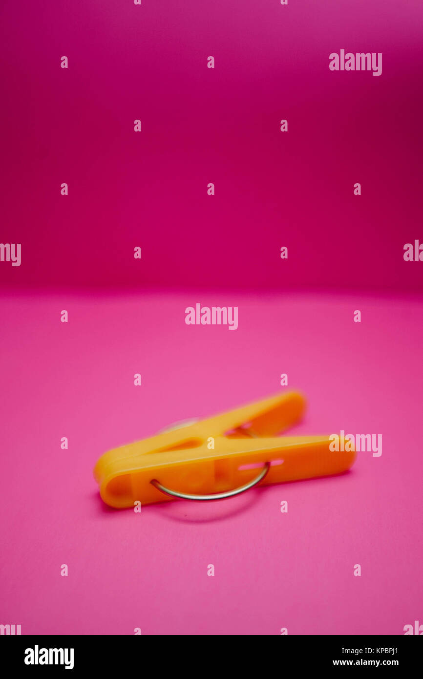 A yellow plastic clothes peg on a one-color pink background. Close up ...