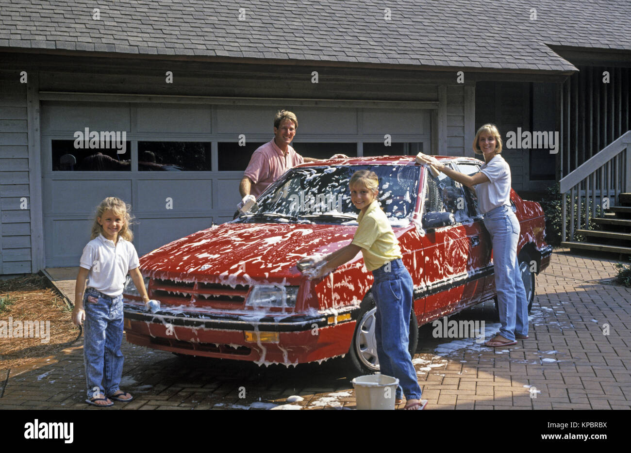 1990 HISTORICAL FAMILY WASHING AUTOMOBILE IN FRONT DRIVEWAY OF SUBURBAN ...