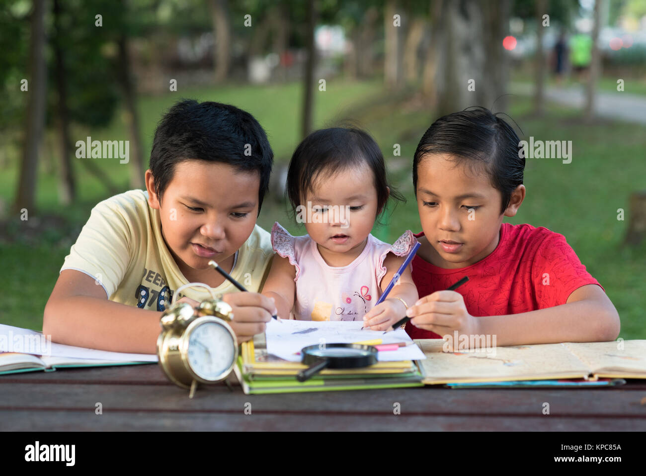 Two asian brothers playing with their little sister drawing together ...