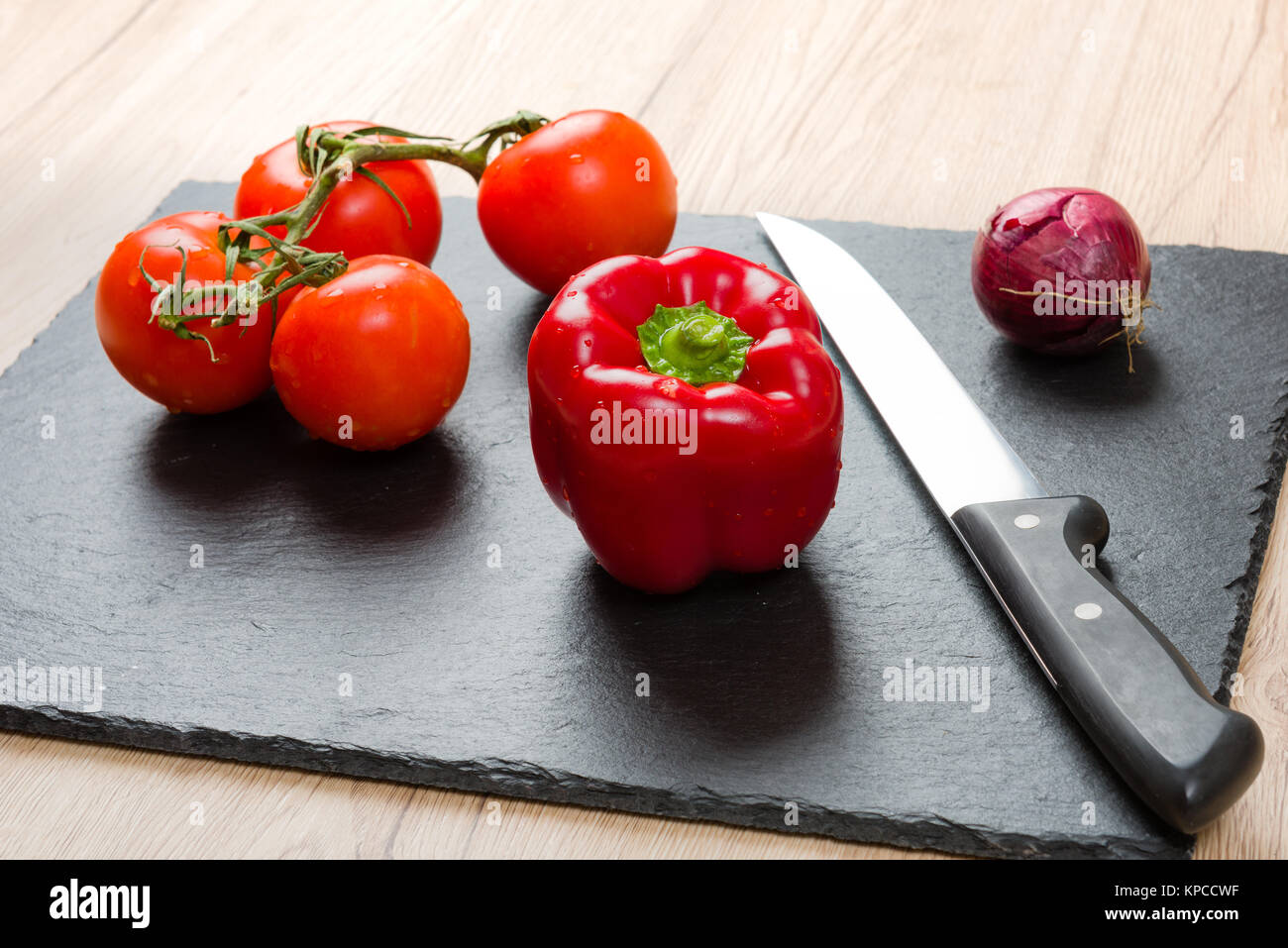 Black slate cutting board with knife and vegetables, ready for slicing ...