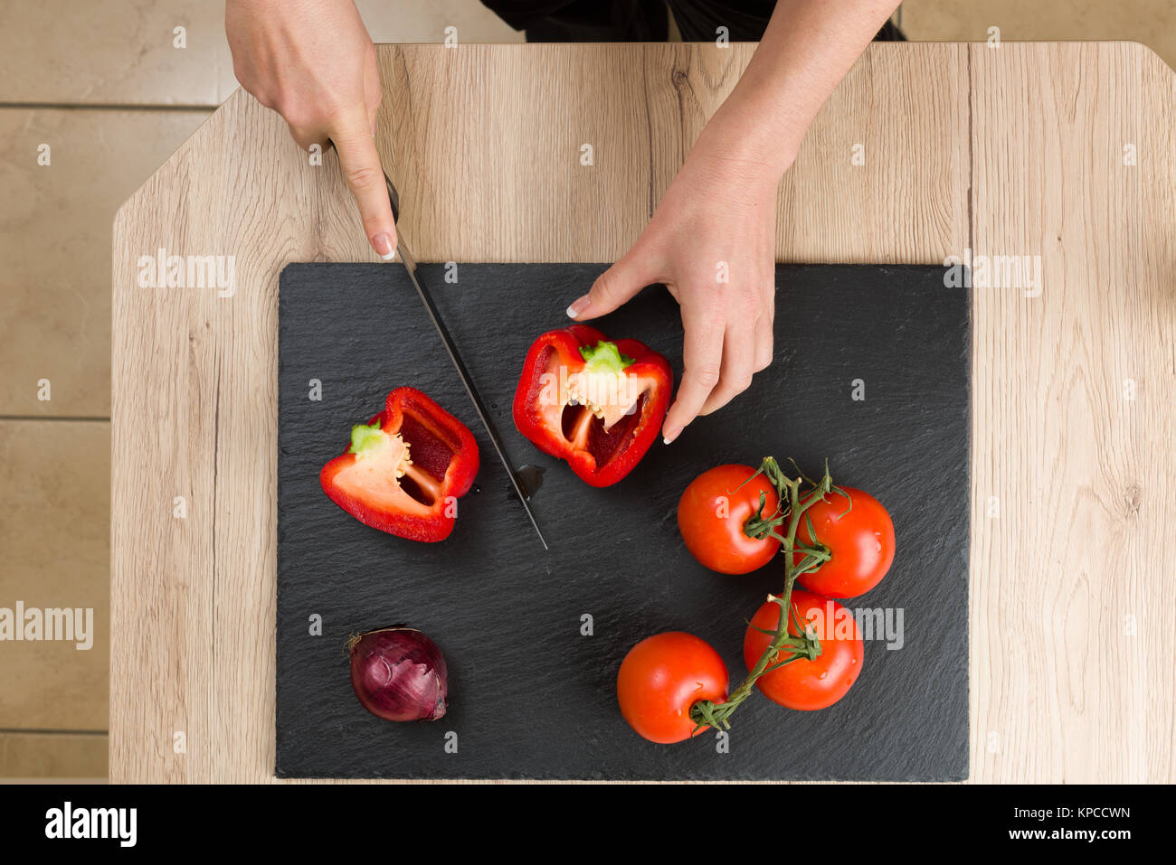 Top down view on black slate cutting board with hands cutting and ...